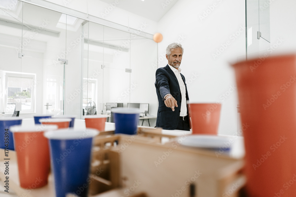 Mature businessman with architectural model in office throwing a ball ...