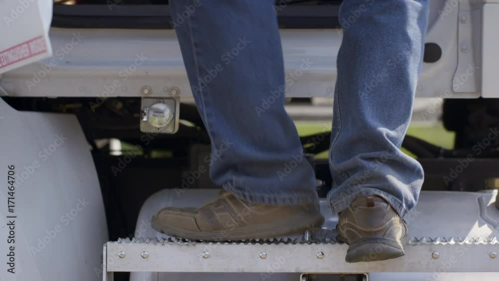 Detail of driver's feet climbing up to truck cab in daylight exterior ...