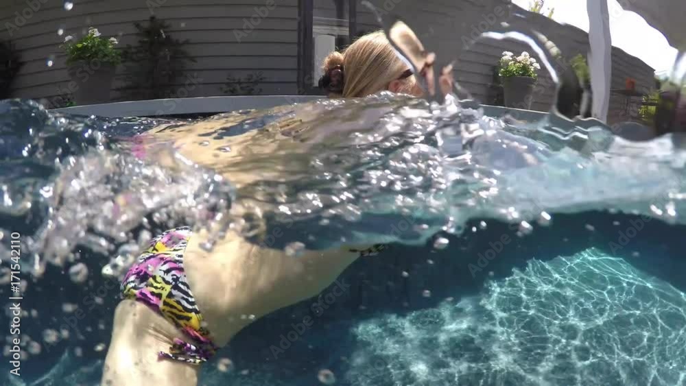 Camera half above and half below water, a beautiful, slim, caucasian woman wearing string bikini ...