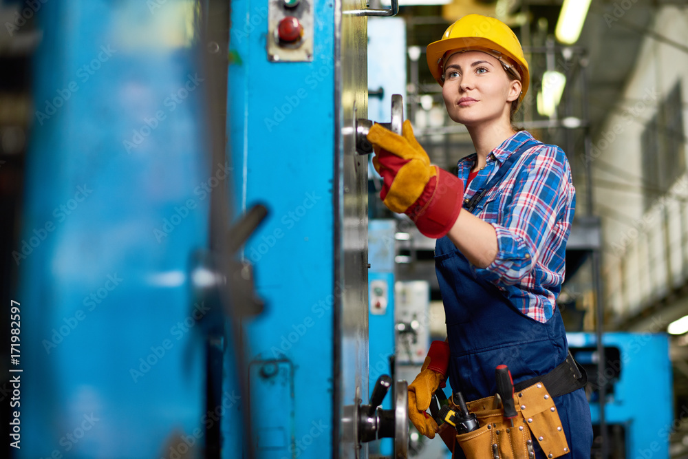 Pretty young machine operator wearing checked shirt and overall ...