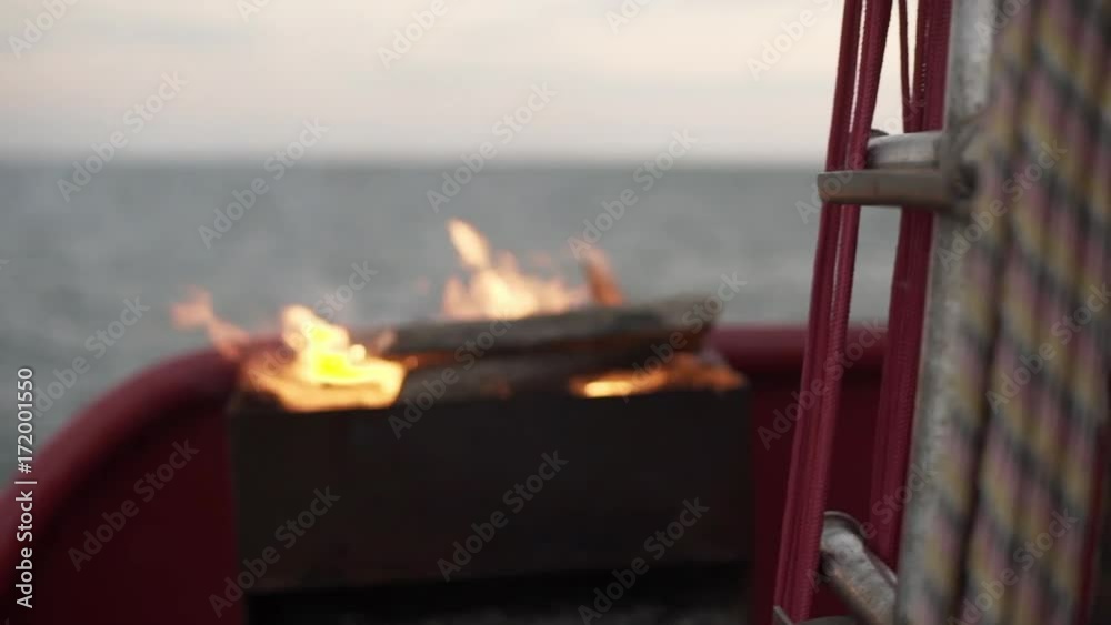 Burning bonfire on a red ship across blue sea, evening lights. Slow ...