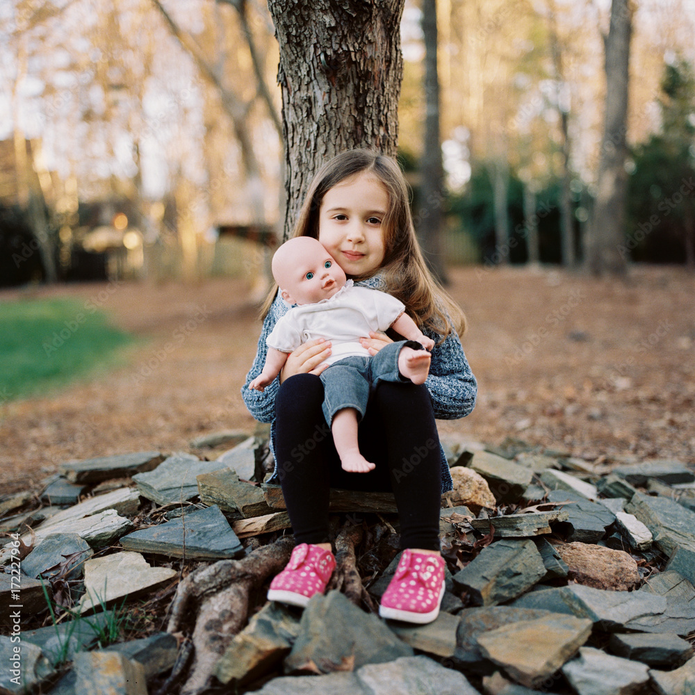 Beautiful young girl sitting by the foot of a tree playing with her ...