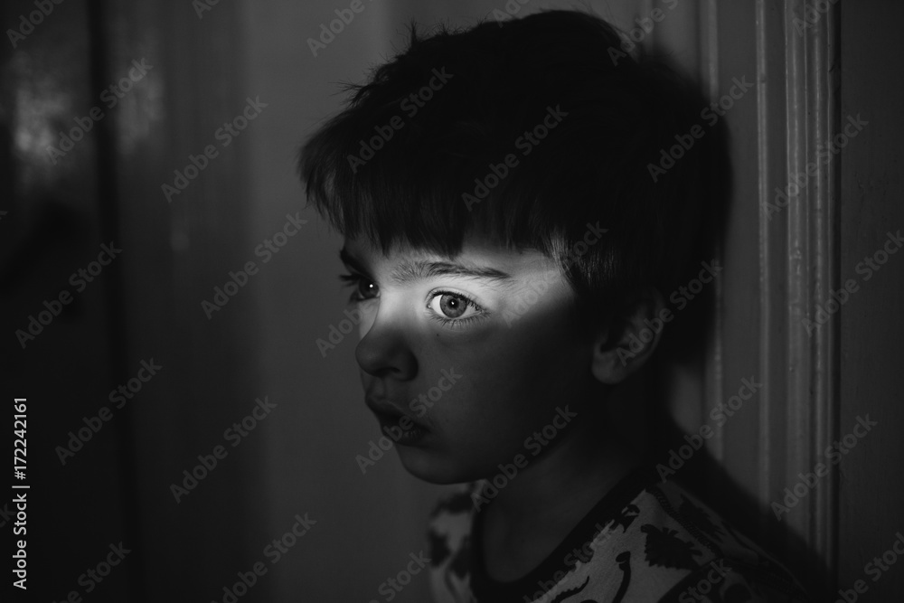 Black and white of boy in dark room with a bright strip of light across ...