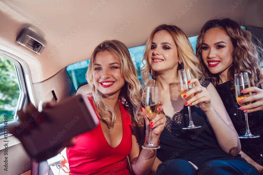 Pretty women having party in a limousine car, drinking champagne and ...