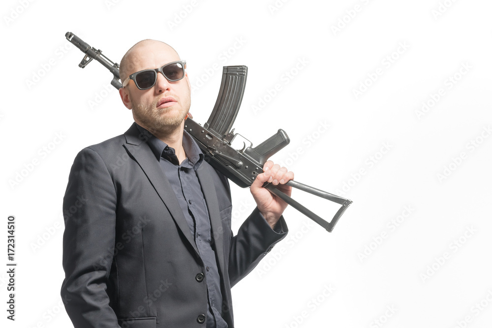 Bald man in a gray suit and sunglasses holding a machine gun on his ...