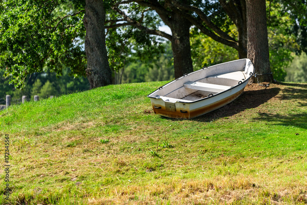 Small plastic rowboat tied to a tree on a small hill on land. No water ...