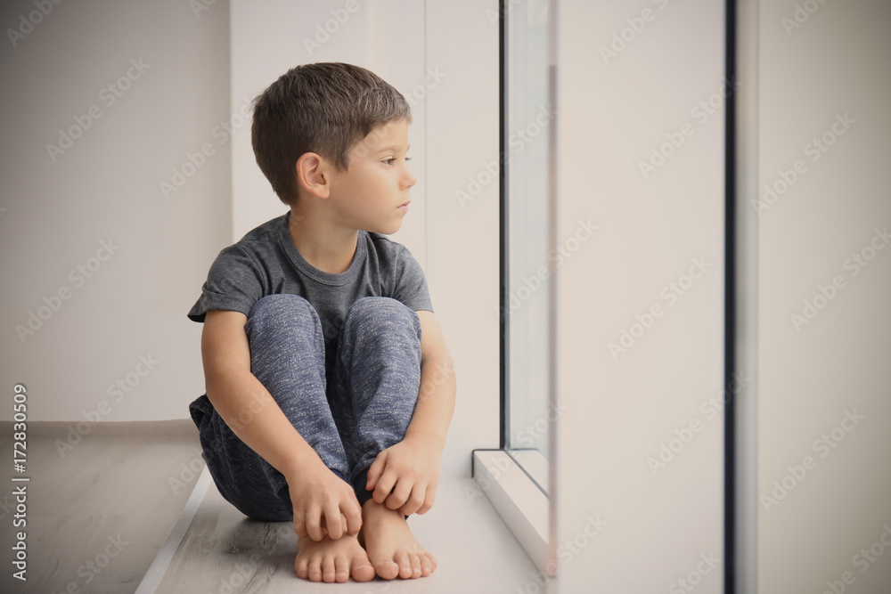 Sad lonely boy sitting on window sill at home Stock Photo | Adobe Stock