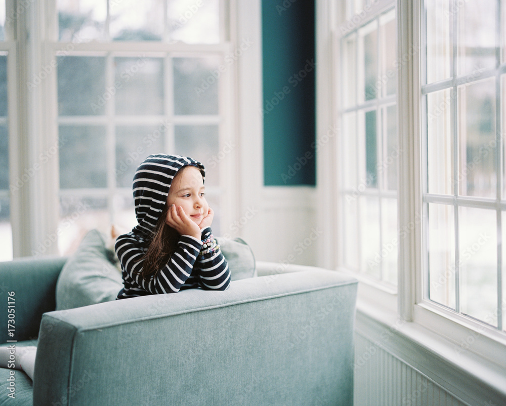 Cute young girl sitting in a chair looking out a window Stock Photo ...