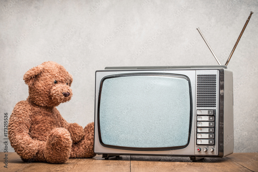 Teddy Bear toy watching retro old TV set receiver on table front ...