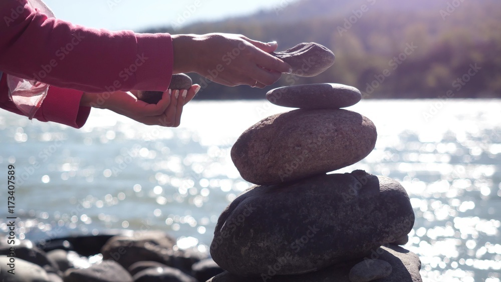 Female hands putting pebble stack next to the mountain river on sunny ...
