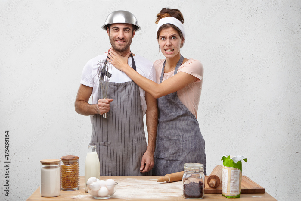 Indoor shot of irritated housewife being busy as cooking, argues with ...