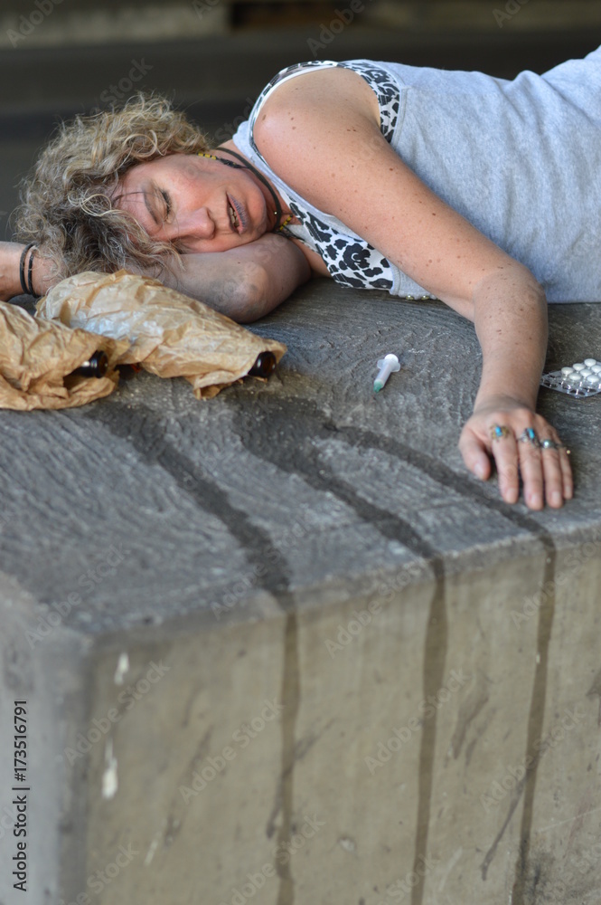 a drunk, homeless woman sleeping under a bridge with bottles of alcohol ...