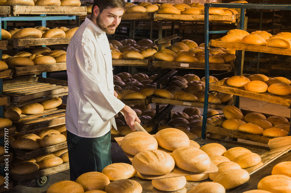 Baker. A young handsome bakery worker on the background of bread, takes ...