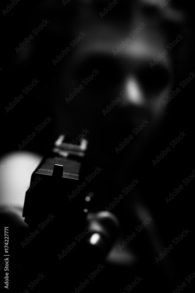 beautiful young woman with gun in dark aiming at camera, blurred ...