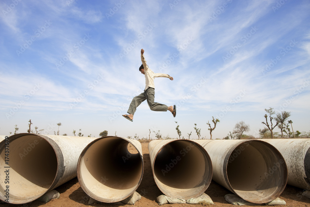 Boy jumping water pipes in desert, India Stock Photo | Adobe Stock