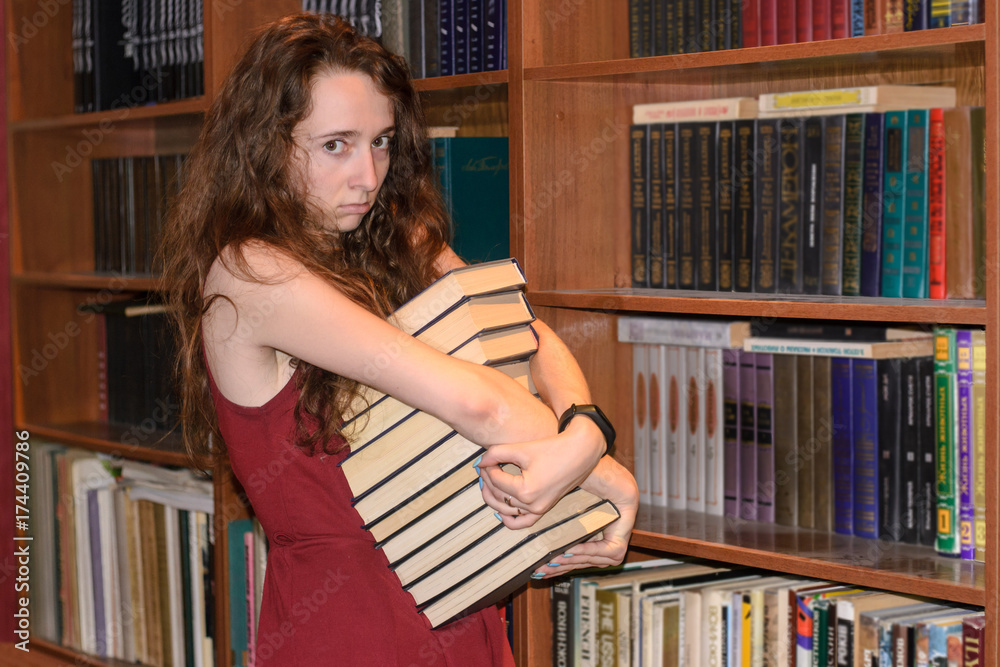 Nice sad girl hardly holds a heavy stack of books with two hands in the ...
