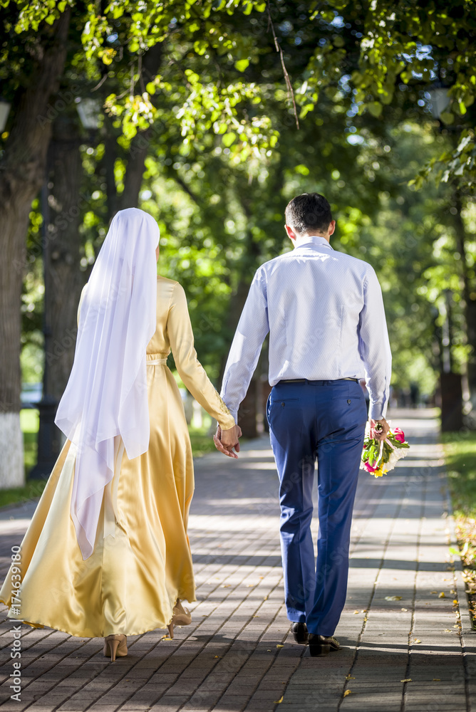 Muslim bride and groom hold hands and walk in the park on a bright ...