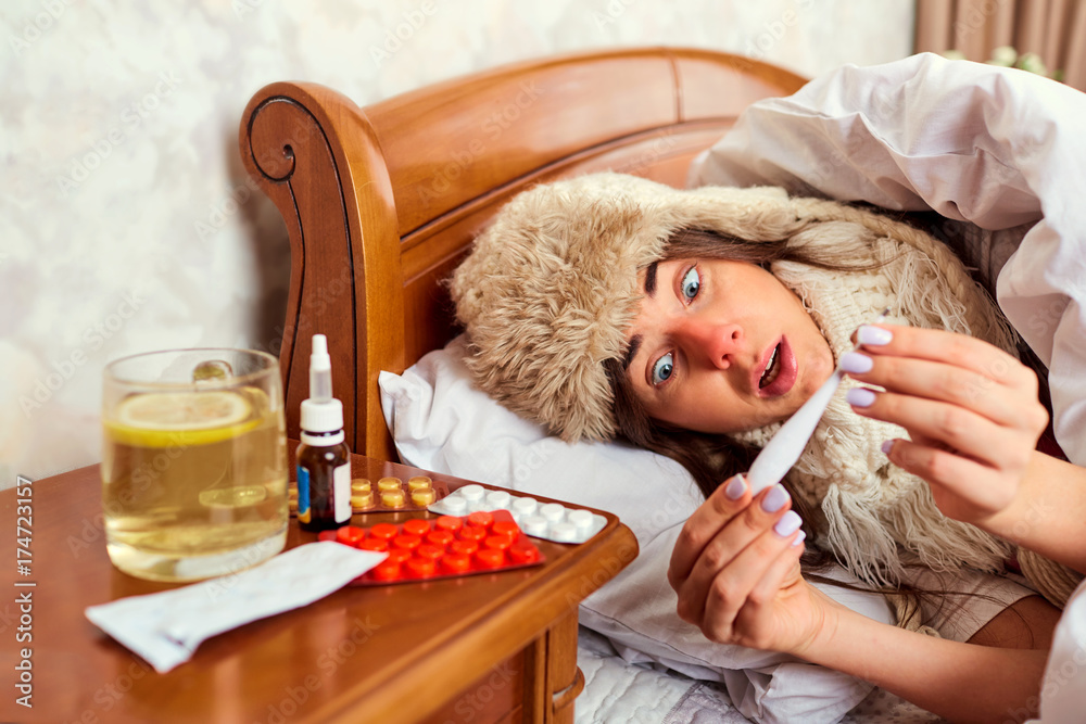 Sick girl lying down looking at thermometer. Stock Photo | Adobe Stock