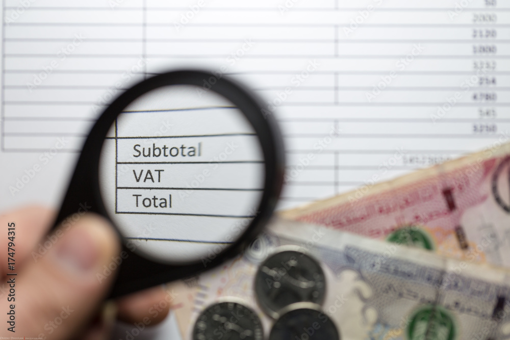 Magnifying glass hold over VAT word. UAE dirhams banknotes and coins on ...