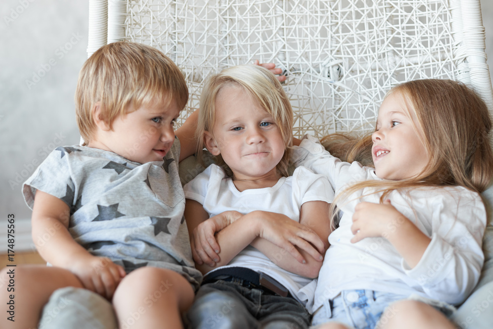 Indoor shot of three little children in basket woven chair, playing ...