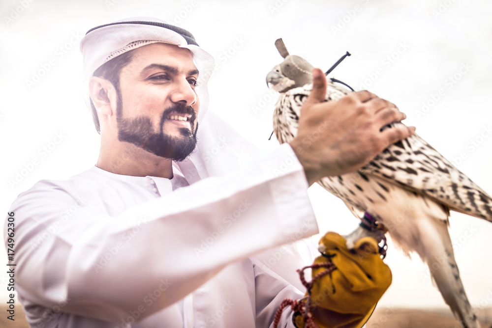 Arabic man with traditional emirates clothes walking in the desert with ...