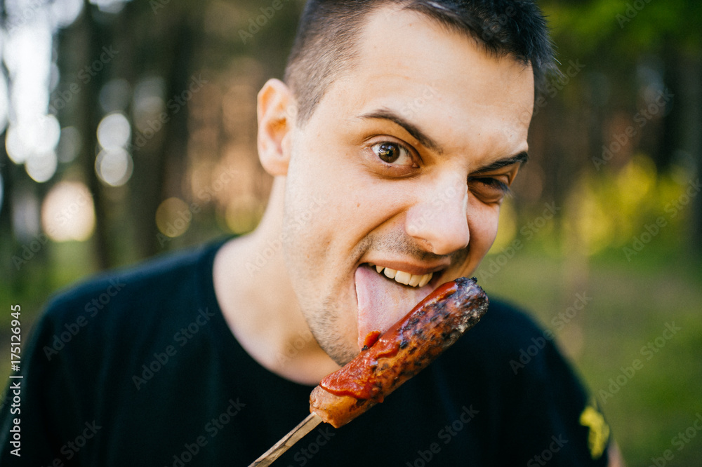 Closeup portrait of male licking and biting roasted sausage with ...