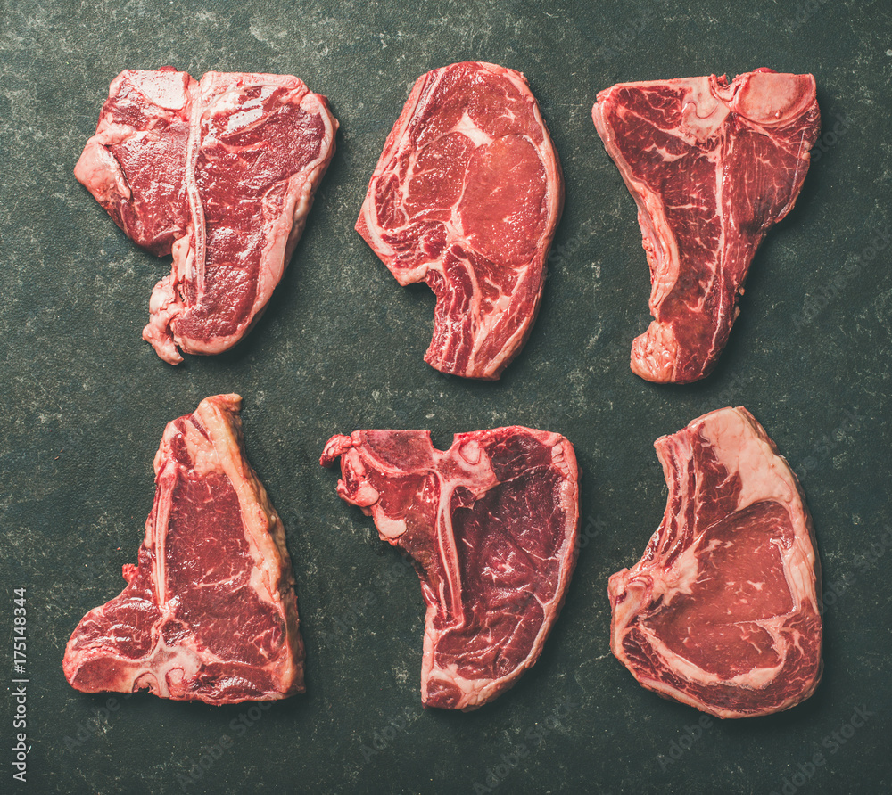Flat-lay of fresh raw beef meat steak cuts over black stone background ...