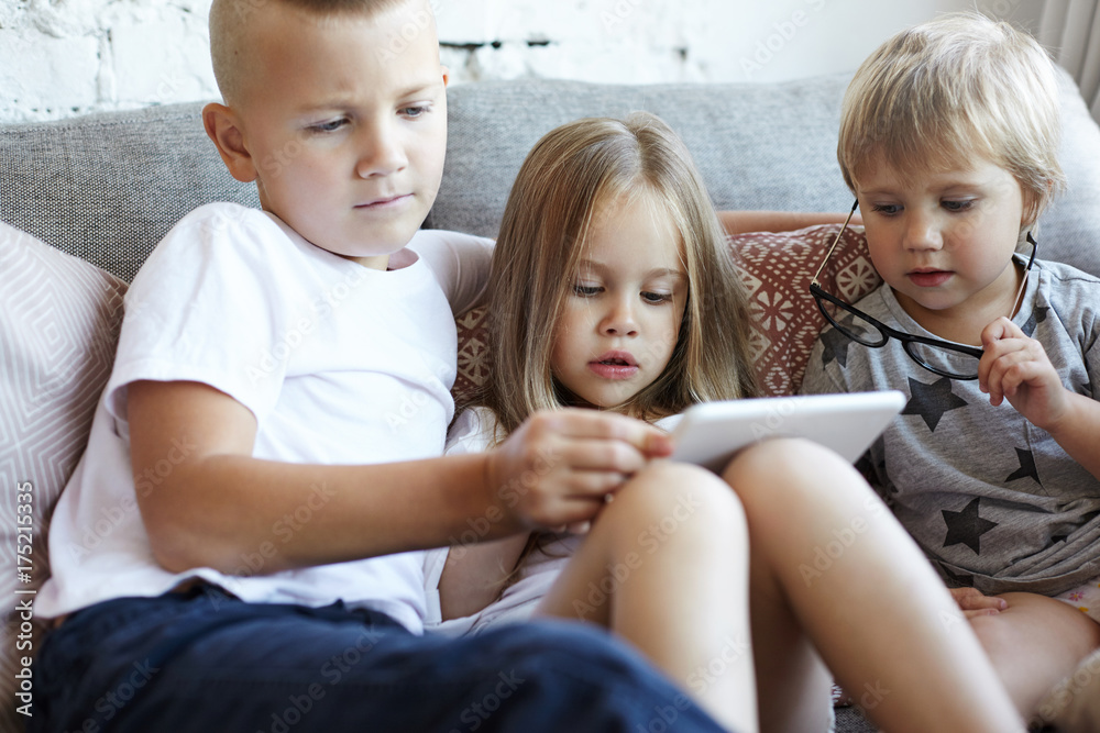 Three siblings watching cartoons online using electronic gadget at home ...