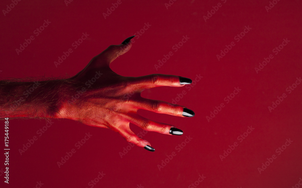 Halloween red devil monster hand with black fingernails against a red ...