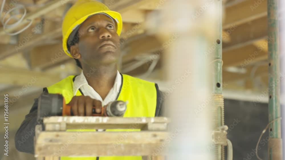 Construction worker on a building site checking roof struts & wiring ...