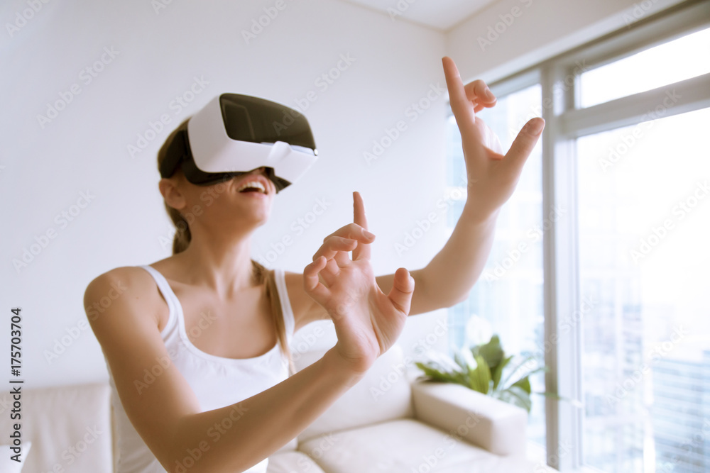 Young excited woman wearing VR headset touching objects in virtual ...
