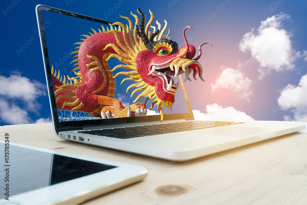 wood office table with red dragon on computer screen and cloud sky ...