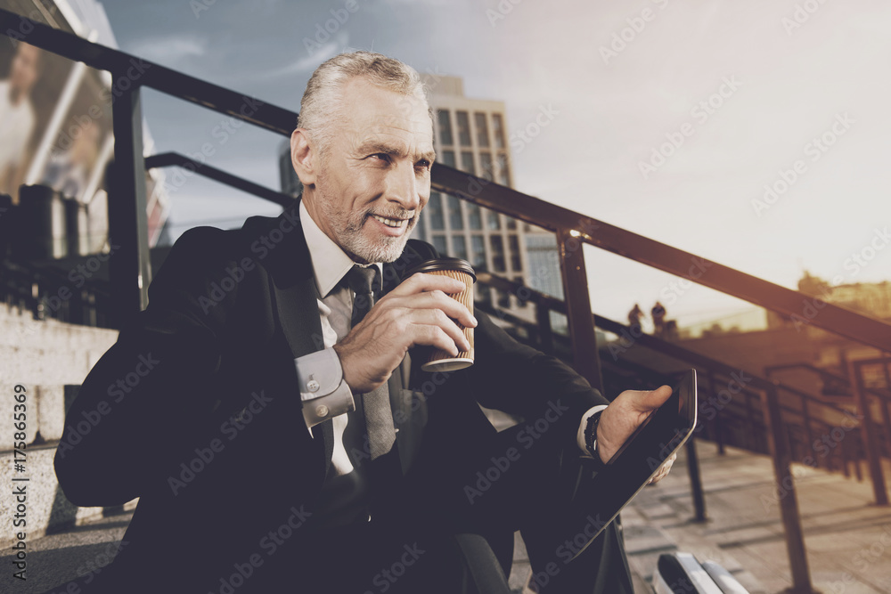 A respectable old man in a strict business suit sits on steps of office ...