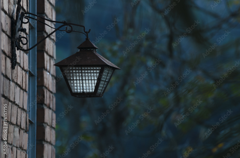 Vintage iron rustic street lamp fixed on a brick wall in dim twilight ...