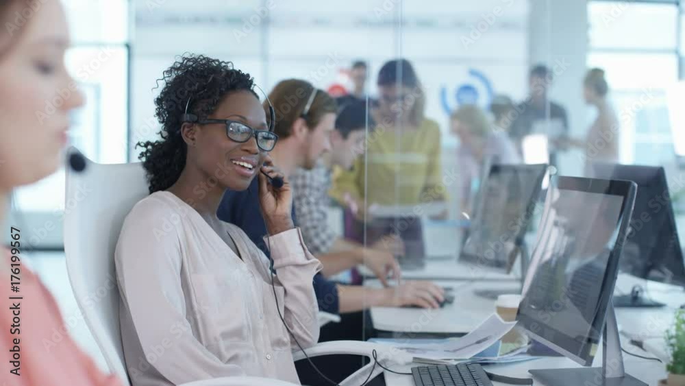 Friendly customer service adviser talking to a customer in busy call ...
