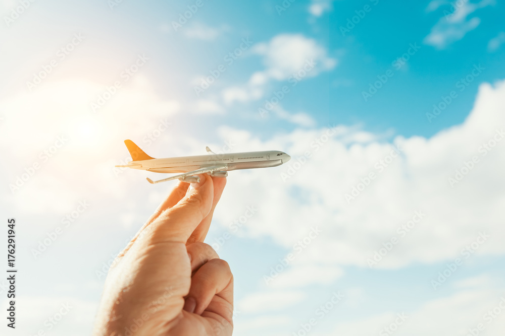 hand holding airplane model in front of cloudy blue sky background. air ...