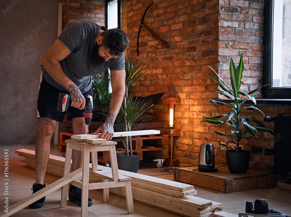 Carpenter drilling a hole in a board in a room with loft interior ...