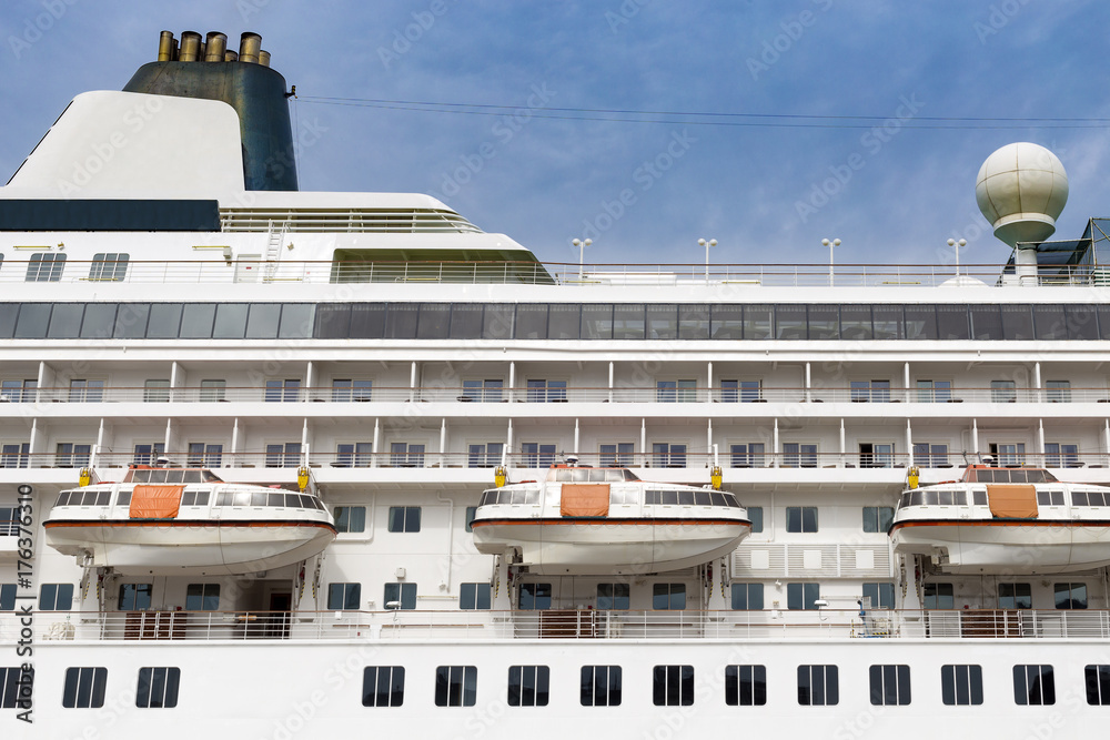 Cruise ship side with lifeboats, windows, stack, radar and blue sky ...