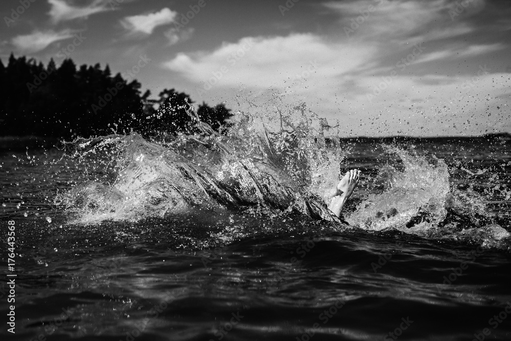Splash caused by a boy jumping into water with his foot visible as he ...