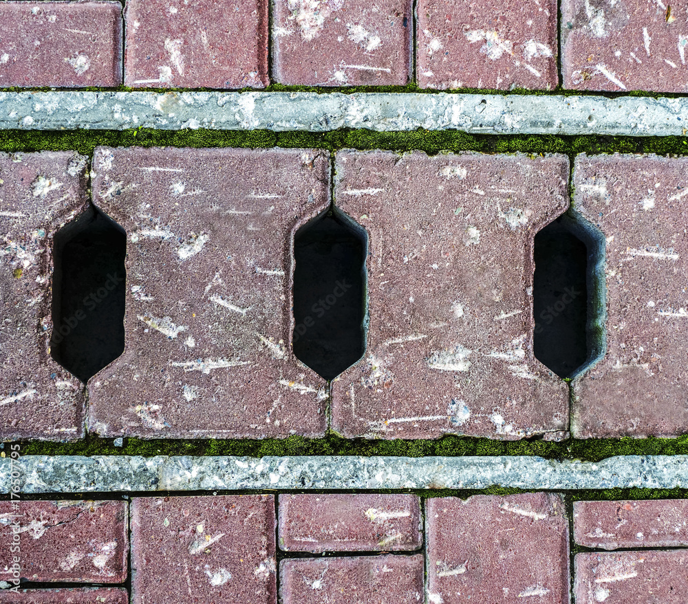 A stretch of road lined with tiles with holes for water flow. An ...