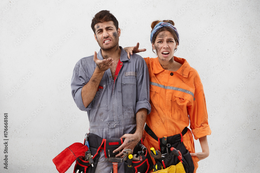 Sad dissatisfied male car mechnic and his pretty wife who helps husband ...
