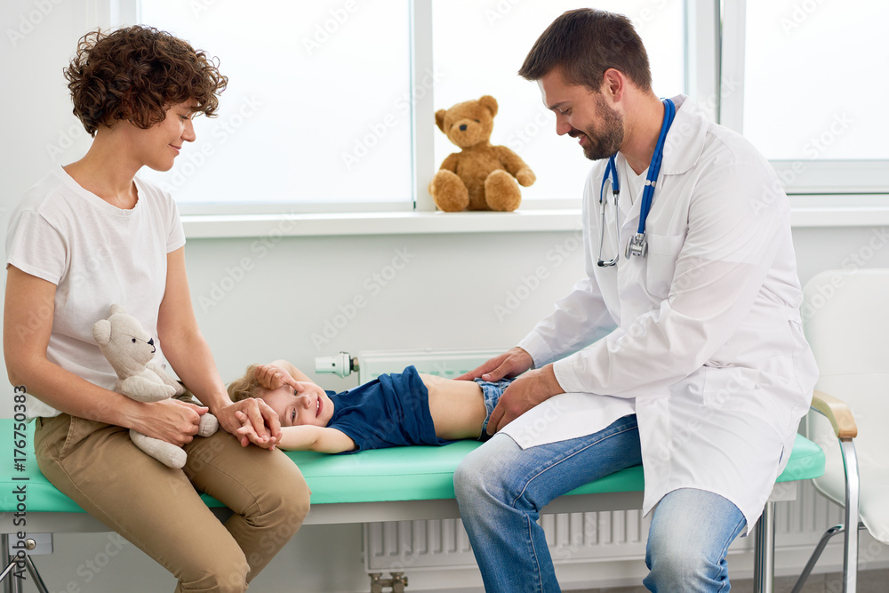 Portrait of smiling doctor examining stomach of little boy palpating in ...