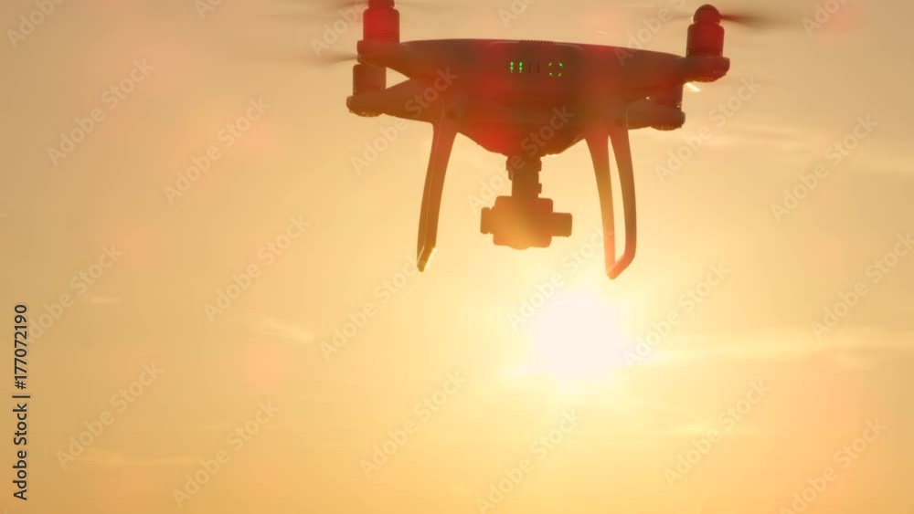CLOSE UP LENS FLARE SILHOUETTE Small filming drone flying over golden ...