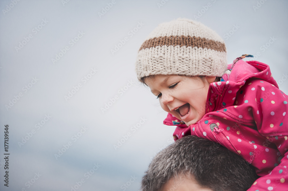 Cute little girl wearing jacket and hat sitting on her father's ...