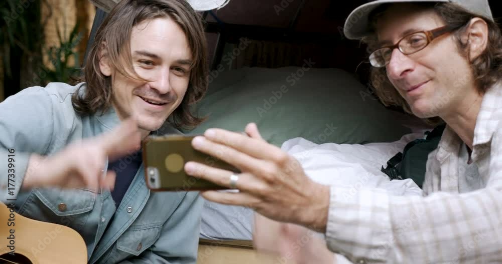 Two handsome men talking selfies with their smart phone camping ...