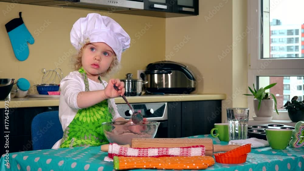 Cute little chef girl with white hat mixing flour for cake on table in ...