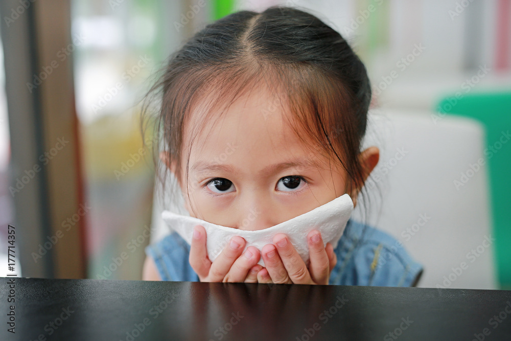 Cute Little asian girl hold a tissues over her mouth. Child looking at ...