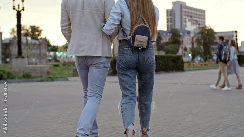 Tilt up rear view of romantic couple holding hands and walking together ...