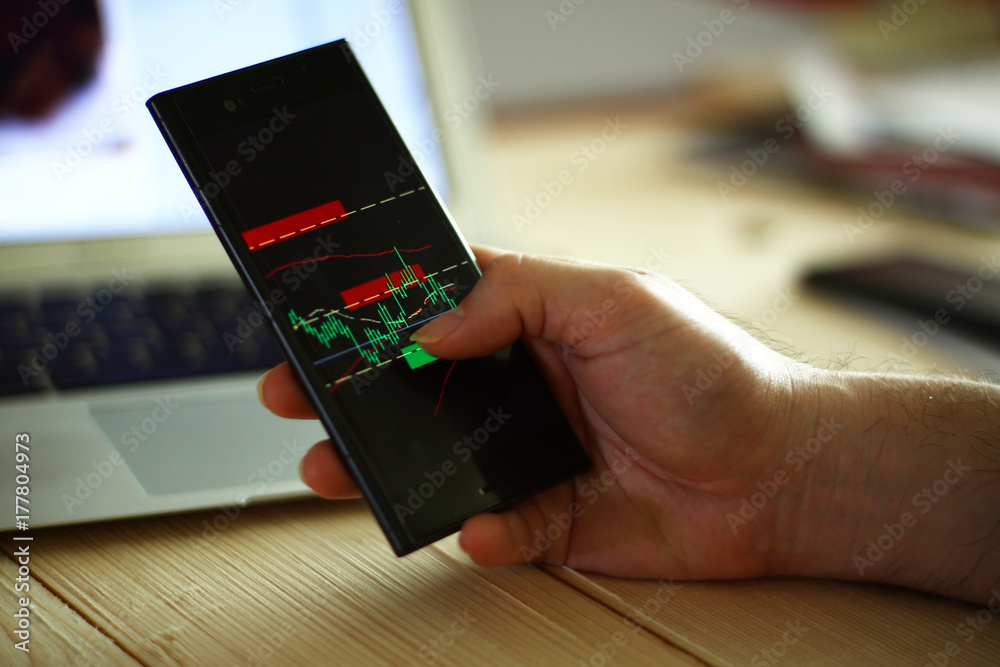 Trader hold smartphone on hand to mornitor chart for trading, financial ...