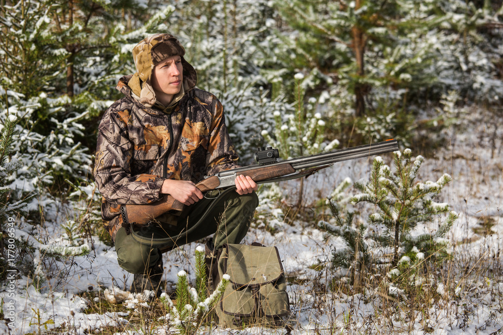 Male hunter in camouflage, armed with a rifle, sitting in a snowy ...